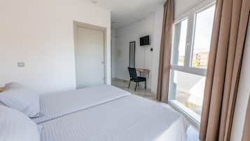 Quarto de hotel com cama, escrivaninha, cadeira, televisão e janela com cortinas.