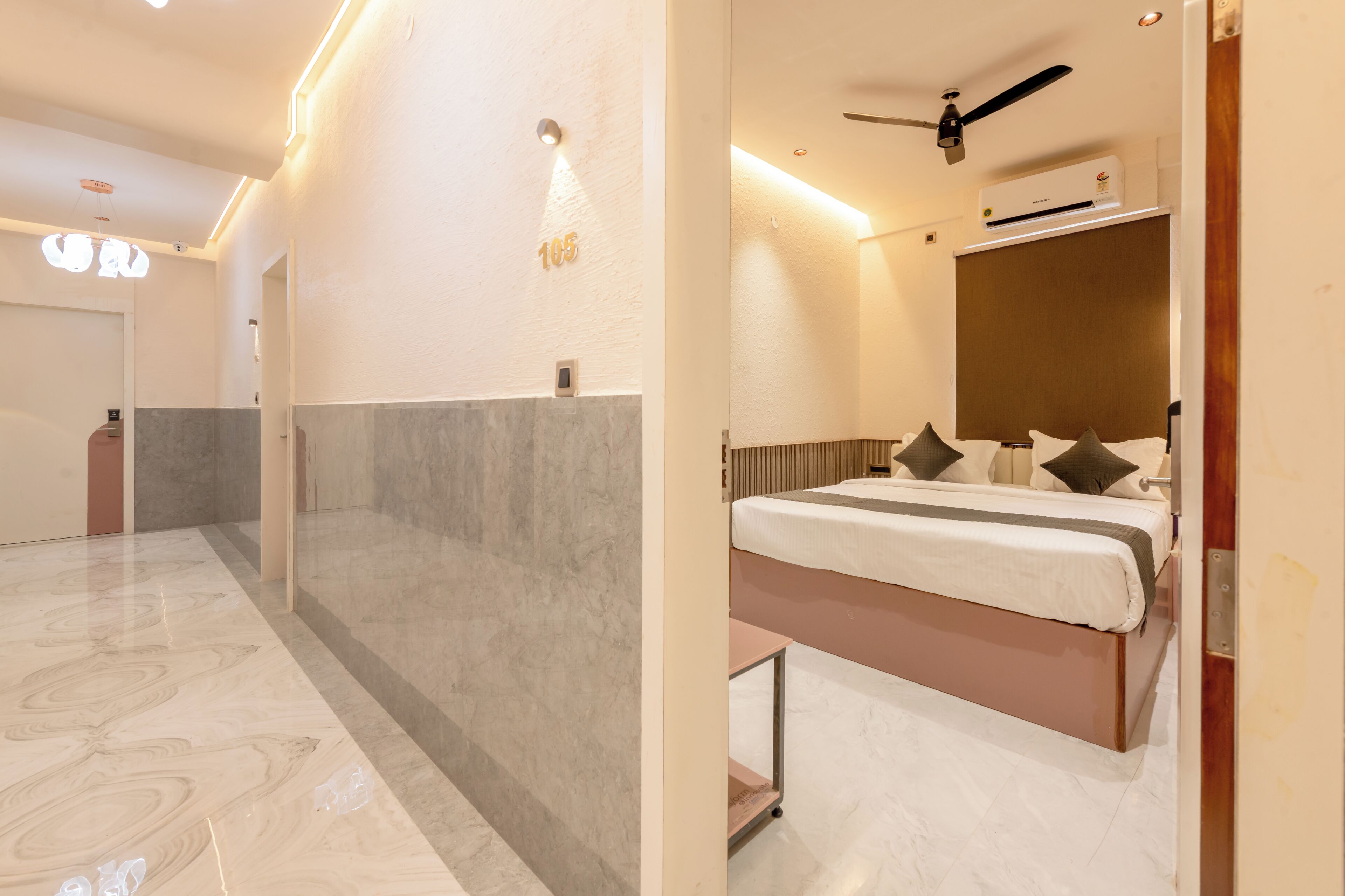 Quarto de hotel com cama, ventilador de teto e banheiro com espelho e porta-toalhas.