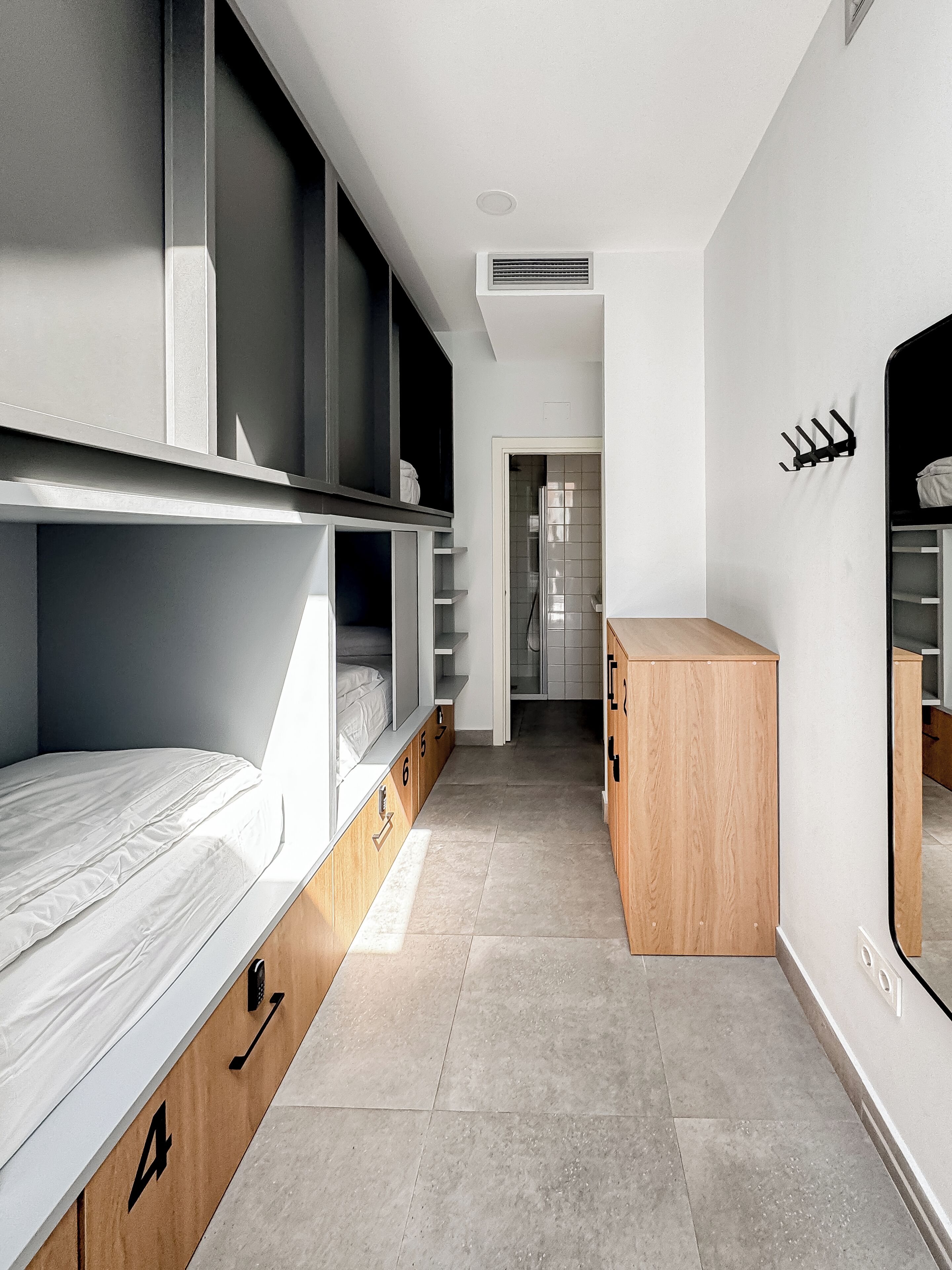 Quarto moderno e minimalista com beliches, um armário de madeira e uma pequena escrivaninha.