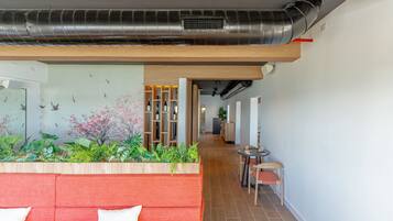 Um interior moderno com um sofá vermelho, um banco de madeira, uma parede de plantas e um corredor que leva a uma sala de jantar.