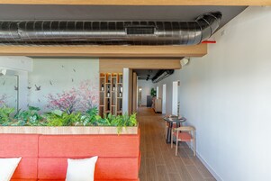 Um interior moderno com um sofá vermelho, um banco de madeira, uma parede de plantas e um corredor que leva a uma sala de jantar.
