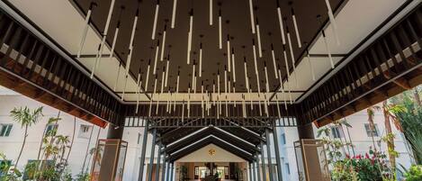 Uma entrada coberta com um caminho central, palmeiras e um edifício com design moderno.