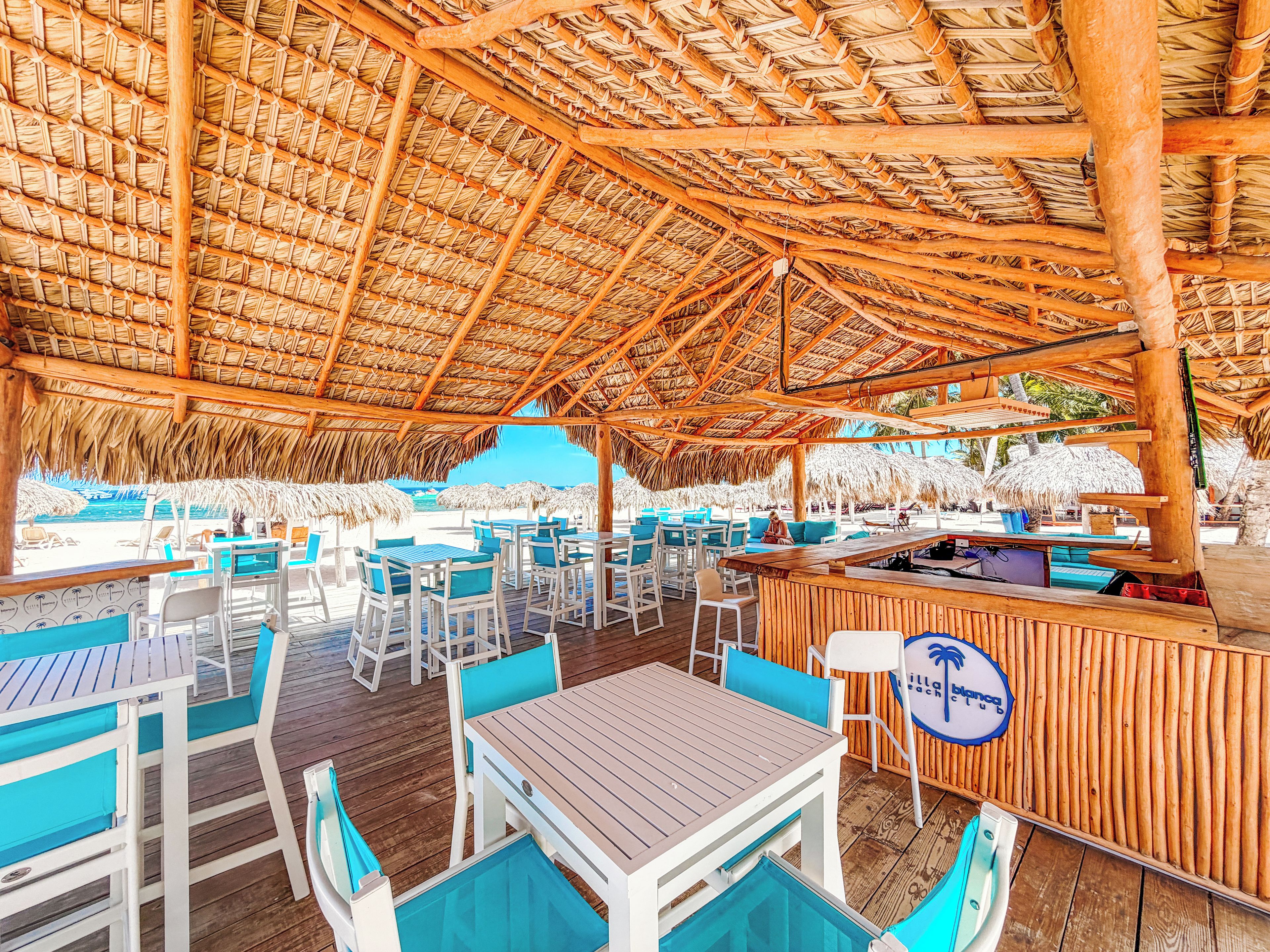 Um restaurante à beira-mar com telhados de palha, mesas ao ar livre e vista para o oceano.