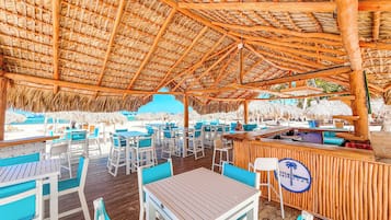Um restaurante à beira-mar com telhados de palha, mesas ao ar livre e vista para o oceano.