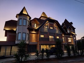 Uma casa de vários andares com uma torre imponente, várias varandas e uma entrada com carros estacionados.