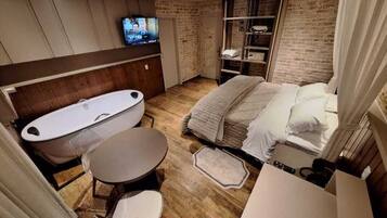 Quarto moderno com cama grande, banheira separada, mesa redonda pequena e televisão.