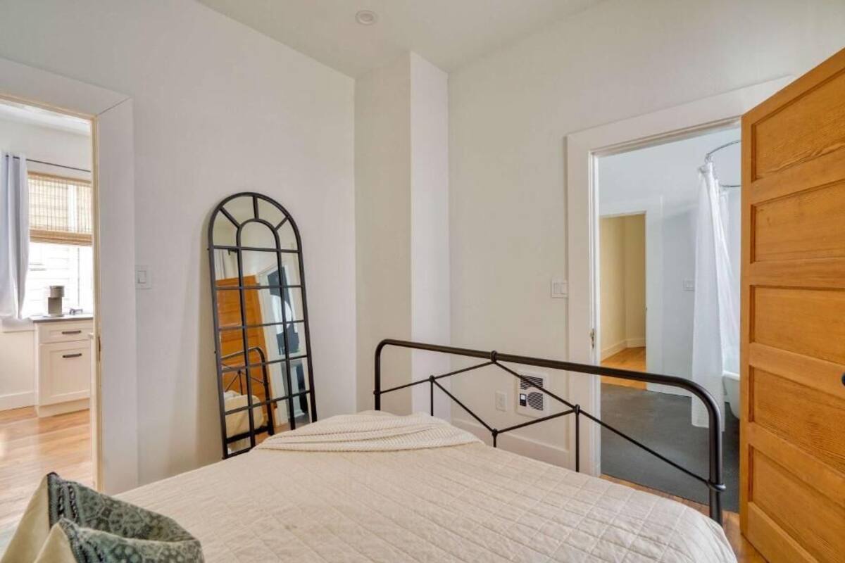 Quarto com cama, porta de madeira, espelho e janela com cortinas.