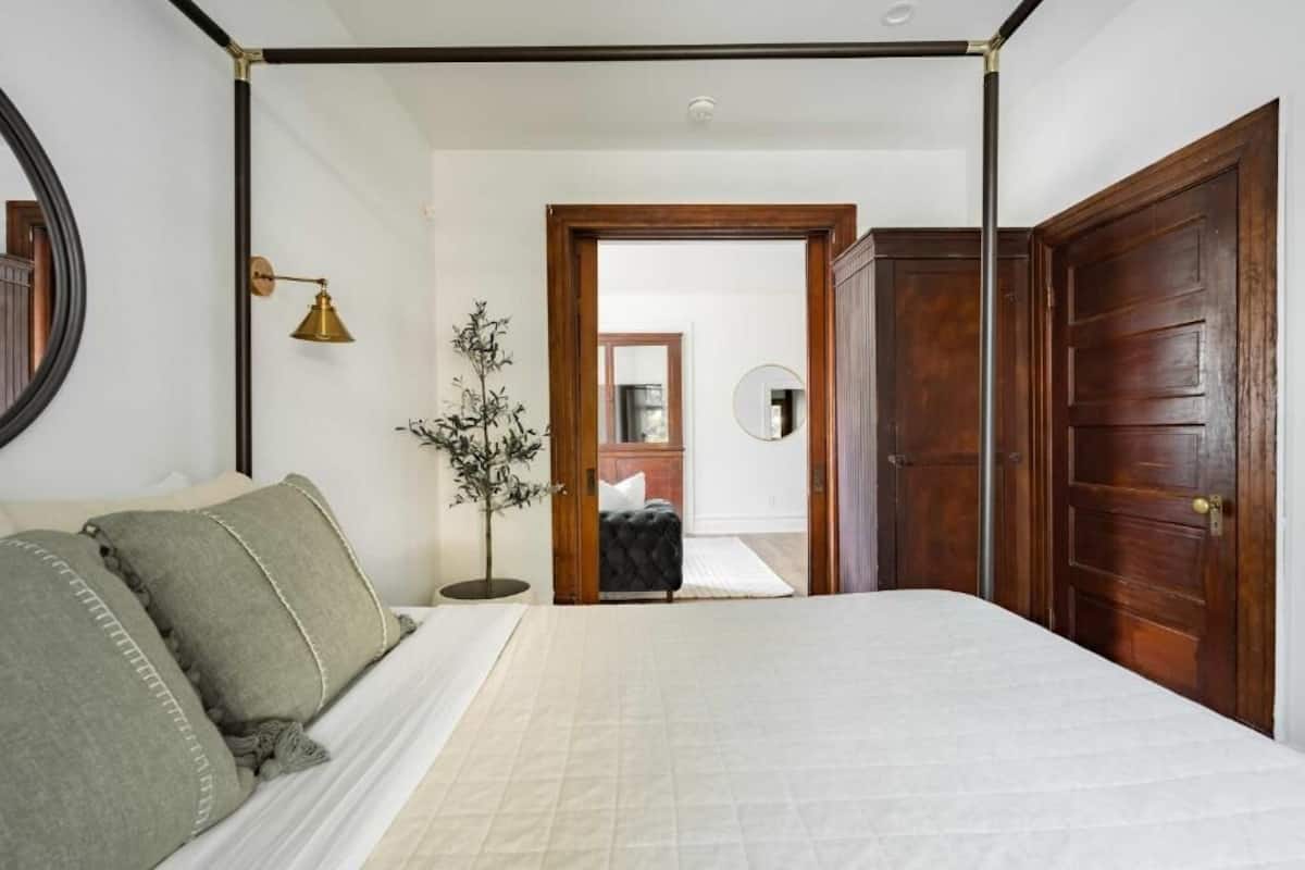 Um quarto com uma cama, abajur, planta e porta de madeira.