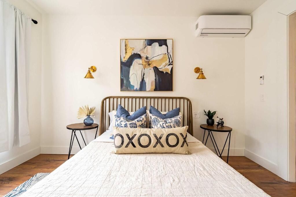 Quarto com cama, cabeceira, ar condicionado fixado na parede e um quadro.