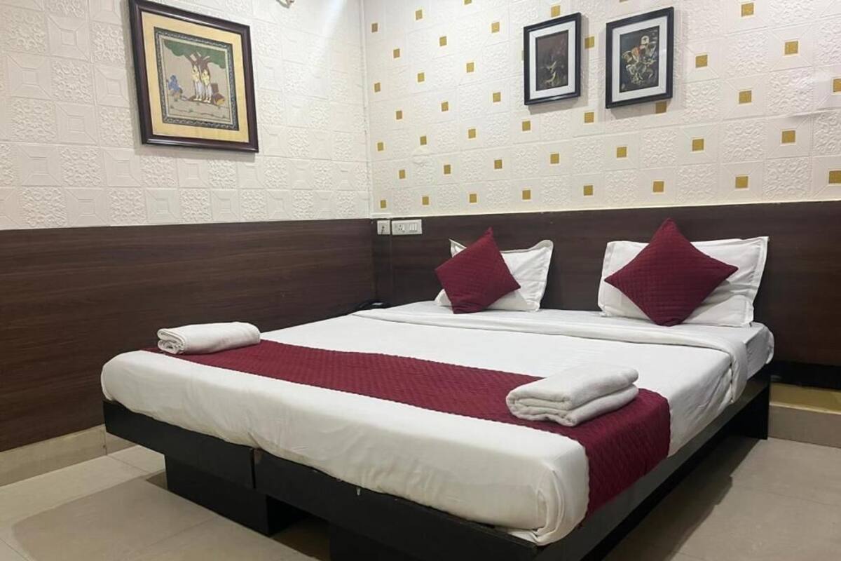 Uma cama bem arrumada com roupa de cama branca e vermelha, duas fotos emolduradas na parede e um padrão decorativo na parede.