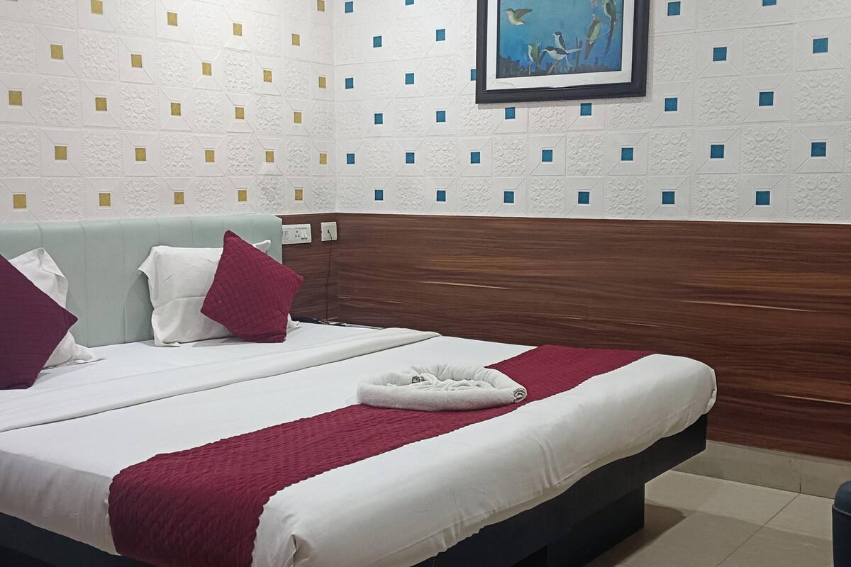Cama bem arrumada com roupa de cama branca e vermelha, cabeceira de madeira e papel de parede estampado.