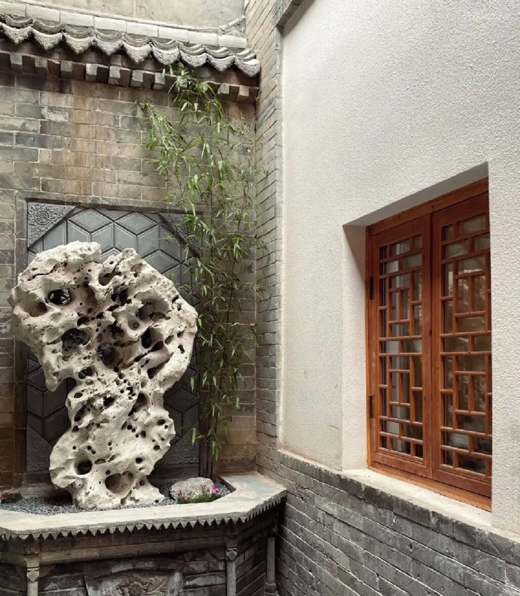 Um pátio tradicional com uma escultura de pedra, bambu e uma janela de madeira.