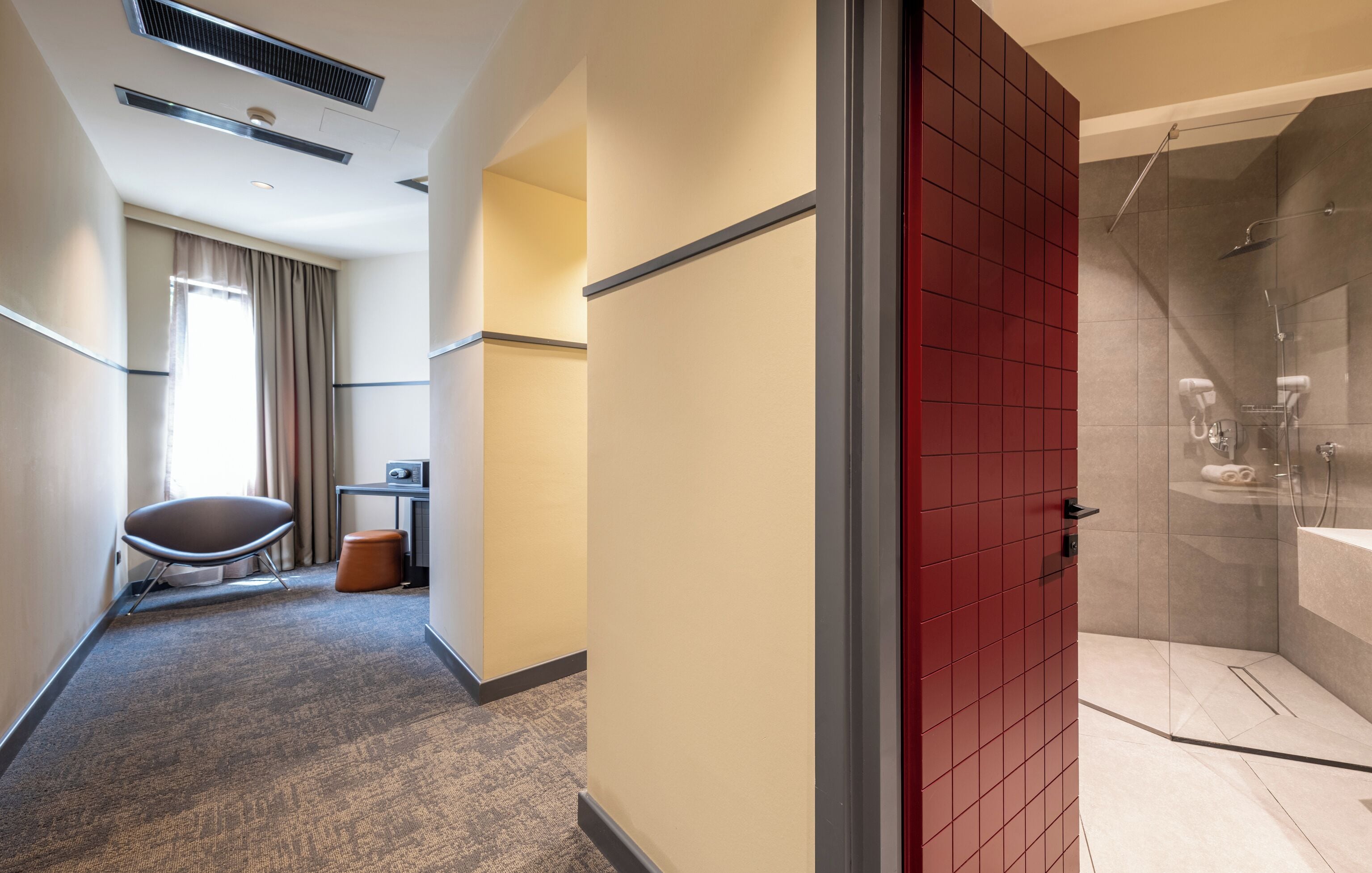 Corredor de hotel com área de chuveiro, uma cadeira e uma pequena mesa.