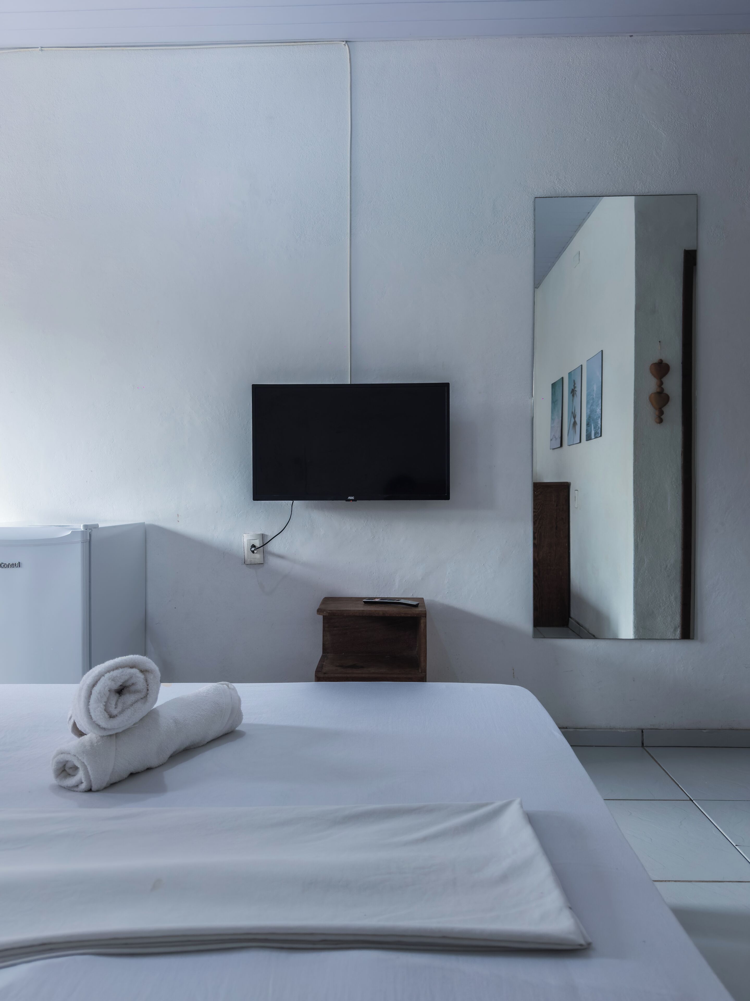 Quarto de hotel moderno com uma cama grande, televisão de tela plana na parede, mesa de cabeceira de madeira e um espelho refletindo o quarto.