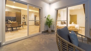 Quarto de hotel moderno com uma grande porta de vidro deslizante que dá para uma área de refeições, um espaço de estar acolhedor com uma cadeira de vime e uma cama bem arrumada.