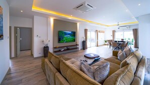 Uma sala de estar moderna com uma televisão de tela plana grande, assentos confortáveis e uma área de jantar com mesa e cadeiras.