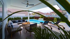 Uma área externa coberta com piscina, espreguiçadeiras e um sofá.