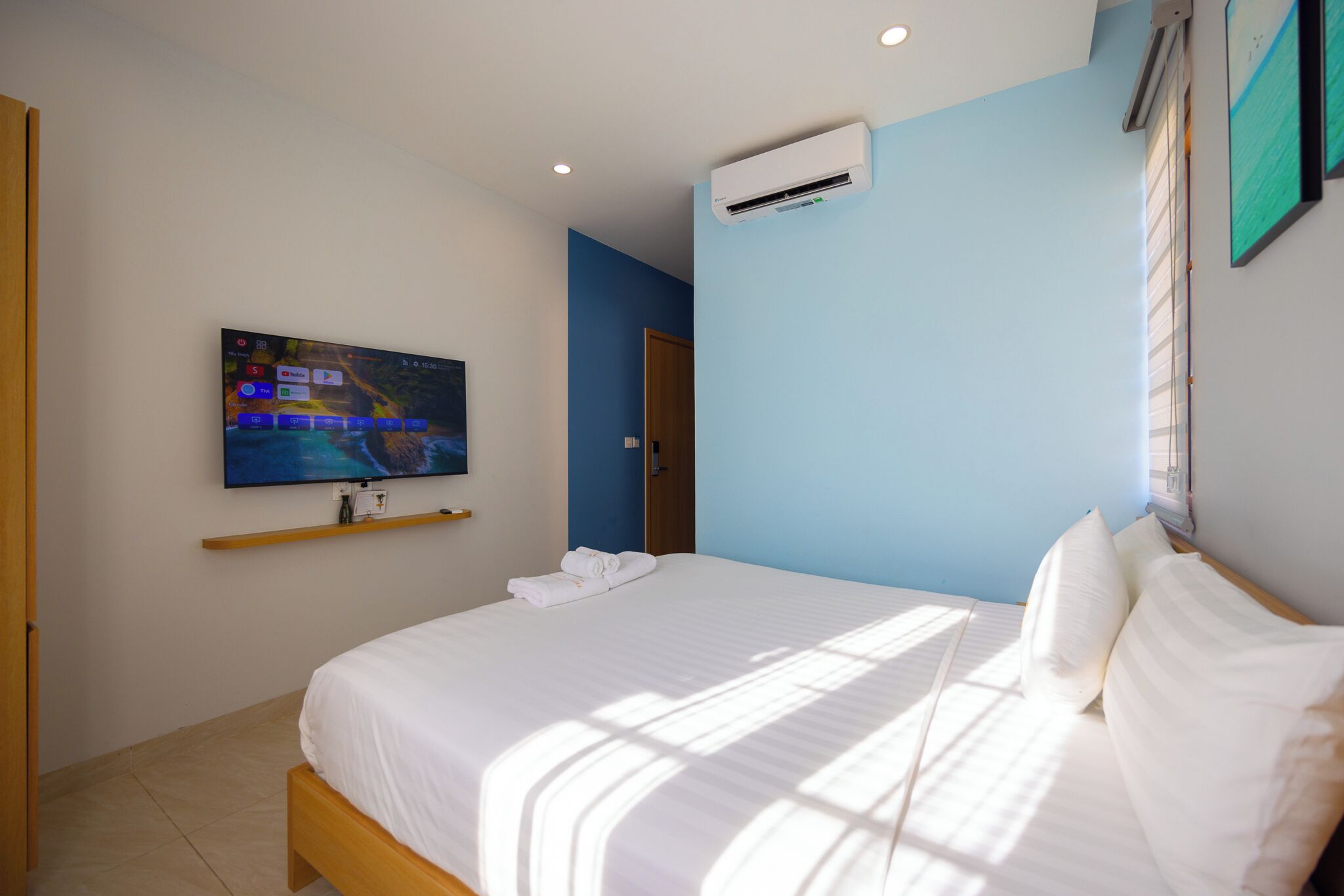 Quarto com cama, televisão na parede, ar condicionado e janela com persianas.