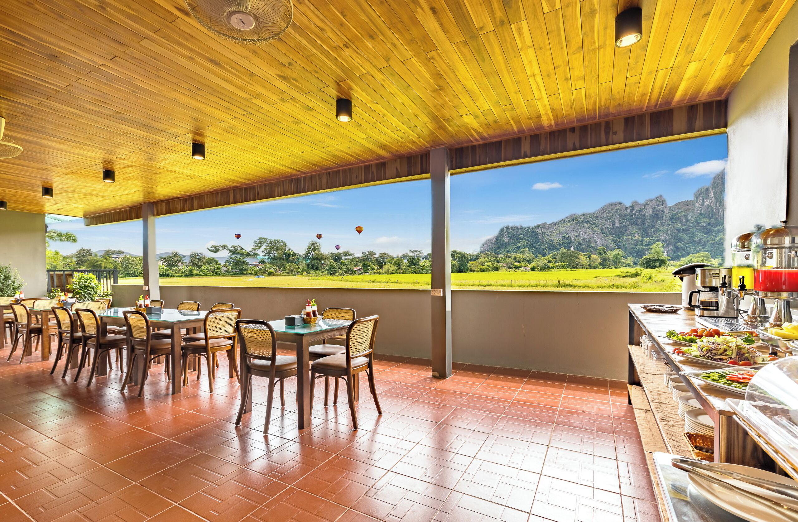 Um restaurante com terraço, teto de madeira e vista para uma paisagem montanhosa.