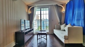 Uma sala de estar moderna com um sofá, uma mesa de centro, uma televisão e vista para edifícios através de grandes janelas.