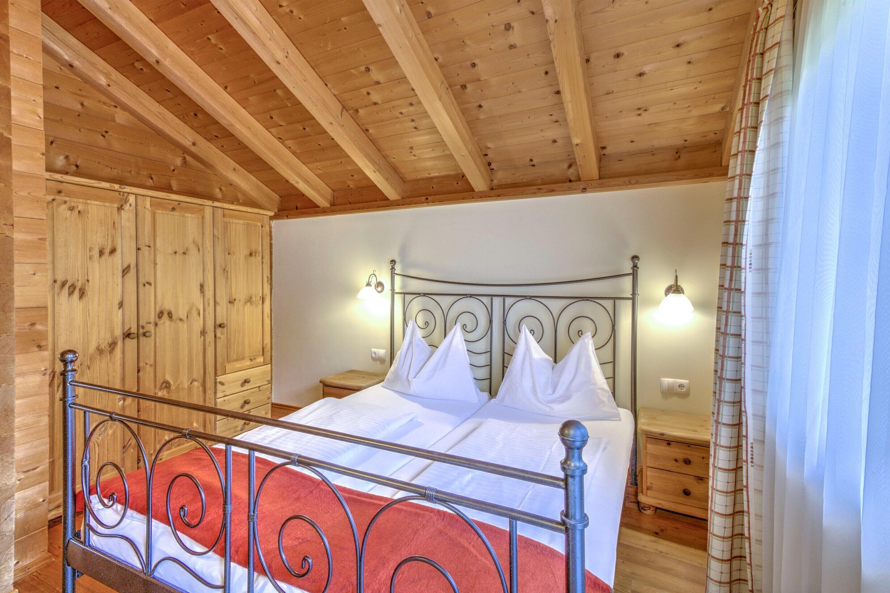 Quarto com painéis de madeira, uma cama com estrutura de metal, uma mesinha de cabeceira de madeira e uma luminária fixada na parede.