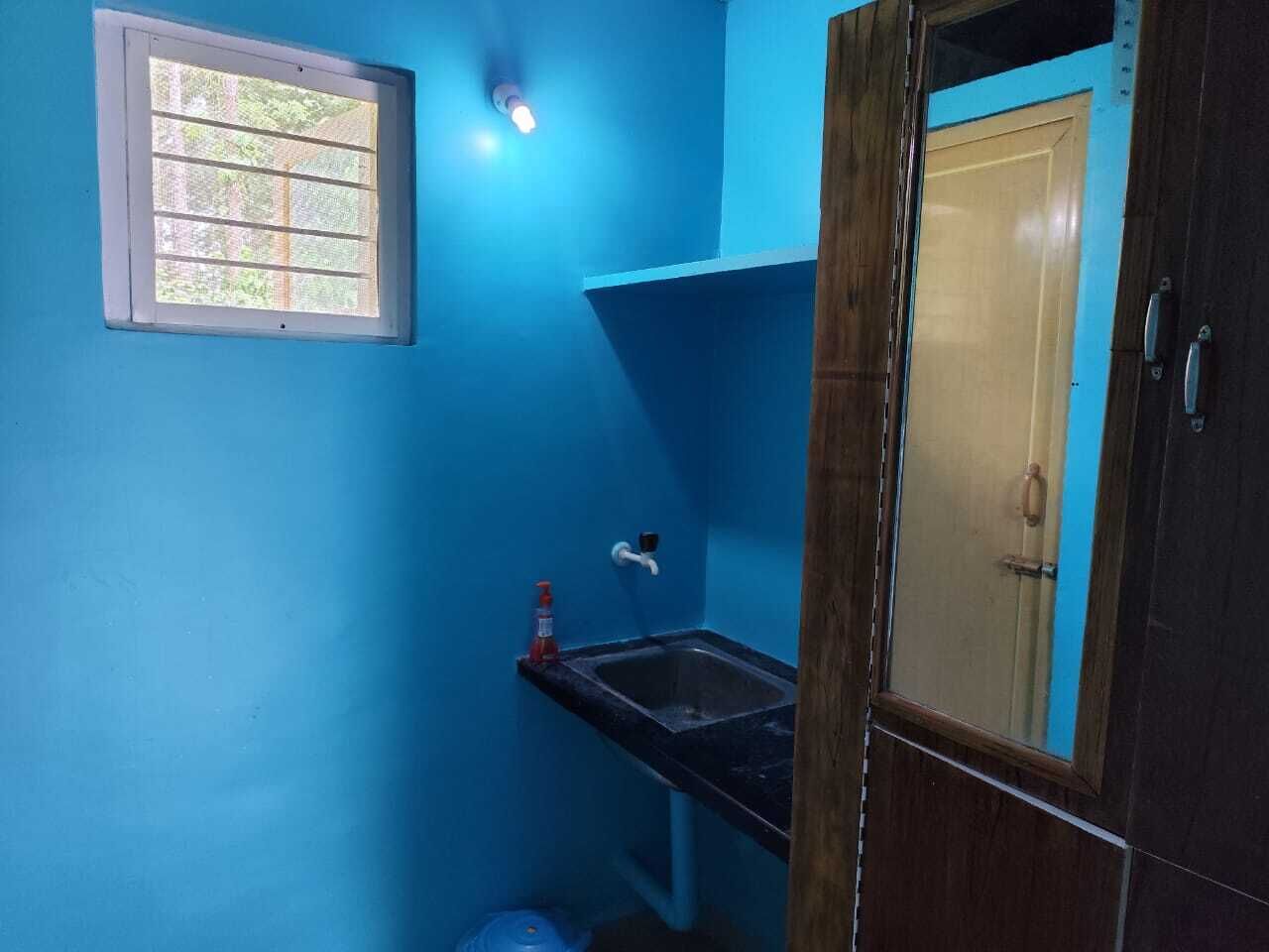 Um banheiro pequeno com parede azul, uma janela com grades, pia com torneira e armário com porta.