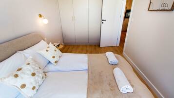 Quarto com cama, almofadas, toalha enrolada, guarda-roupa e luminária fixada na parede.
