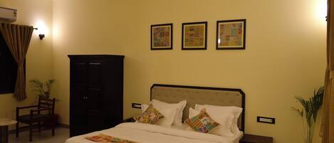 Quarto de hotel com cama, mesa de cabeceira, cadeira, guarda-roupa e três quadros na parede.
