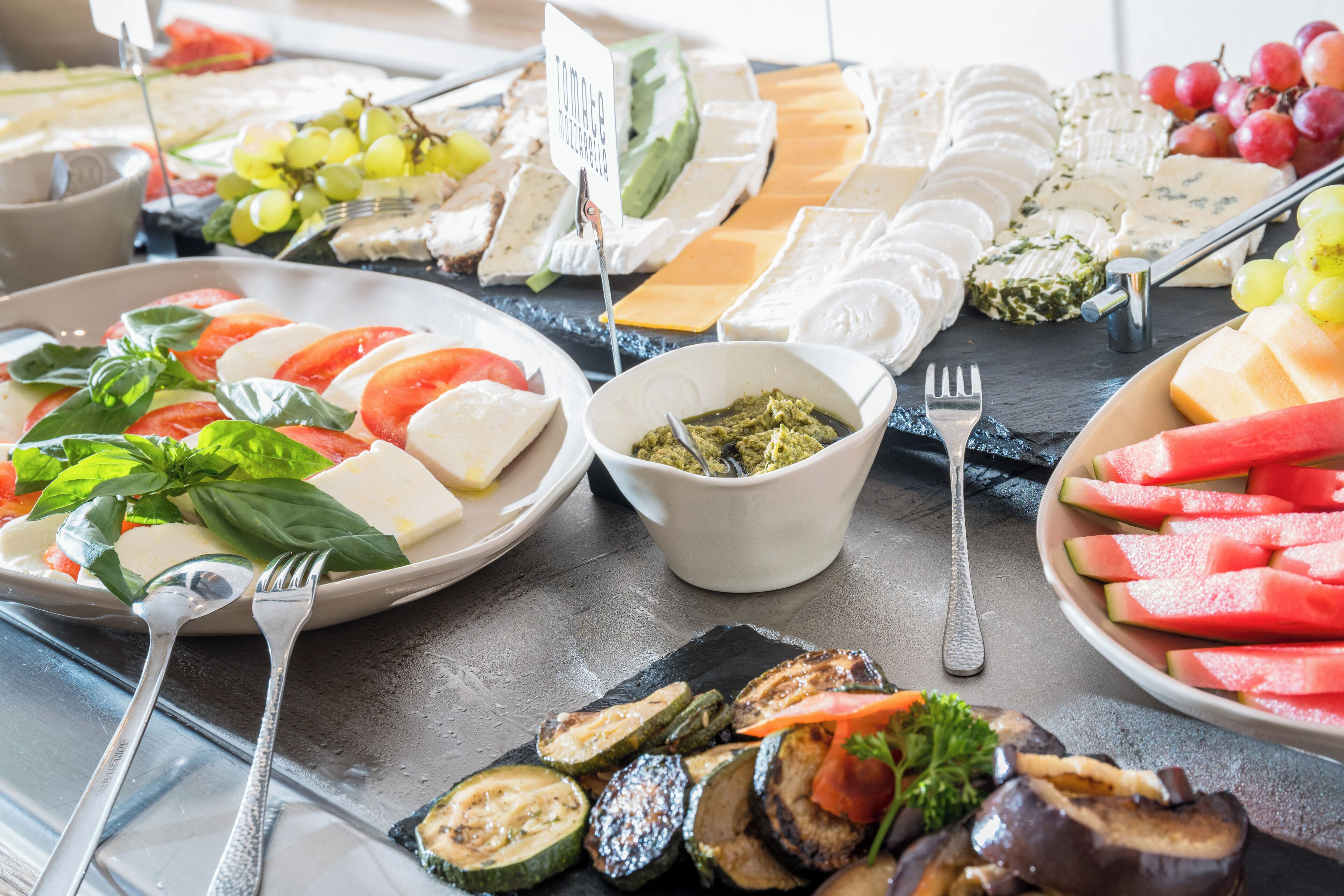 Um buffet com diversos queijos, frutas e legumes.