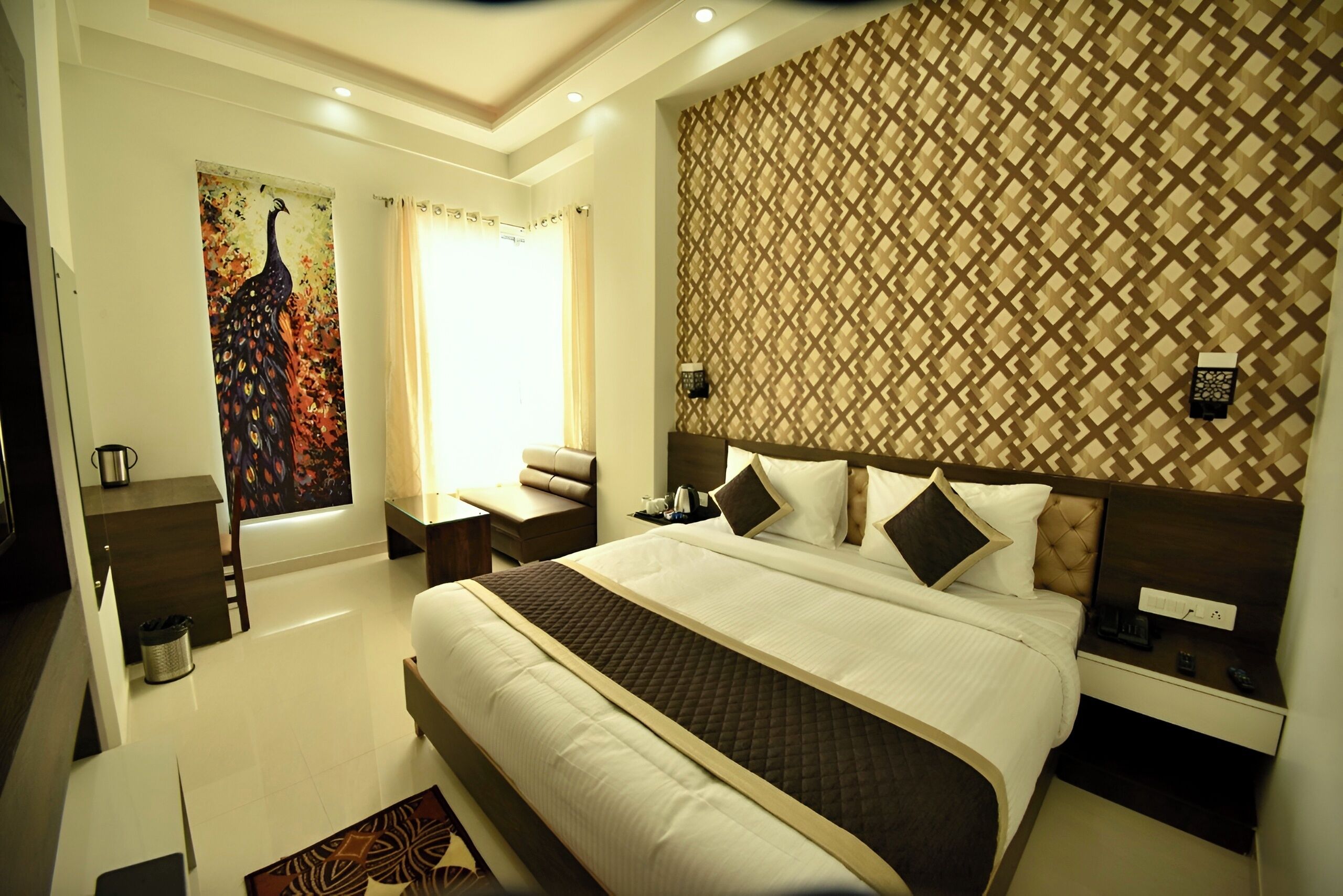 Quarto de hotel com uma cama grande, uma escrivaninha, uma cadeira, uma mesa de cabeceira, uma luminária na parede e uma janela com cortinas.