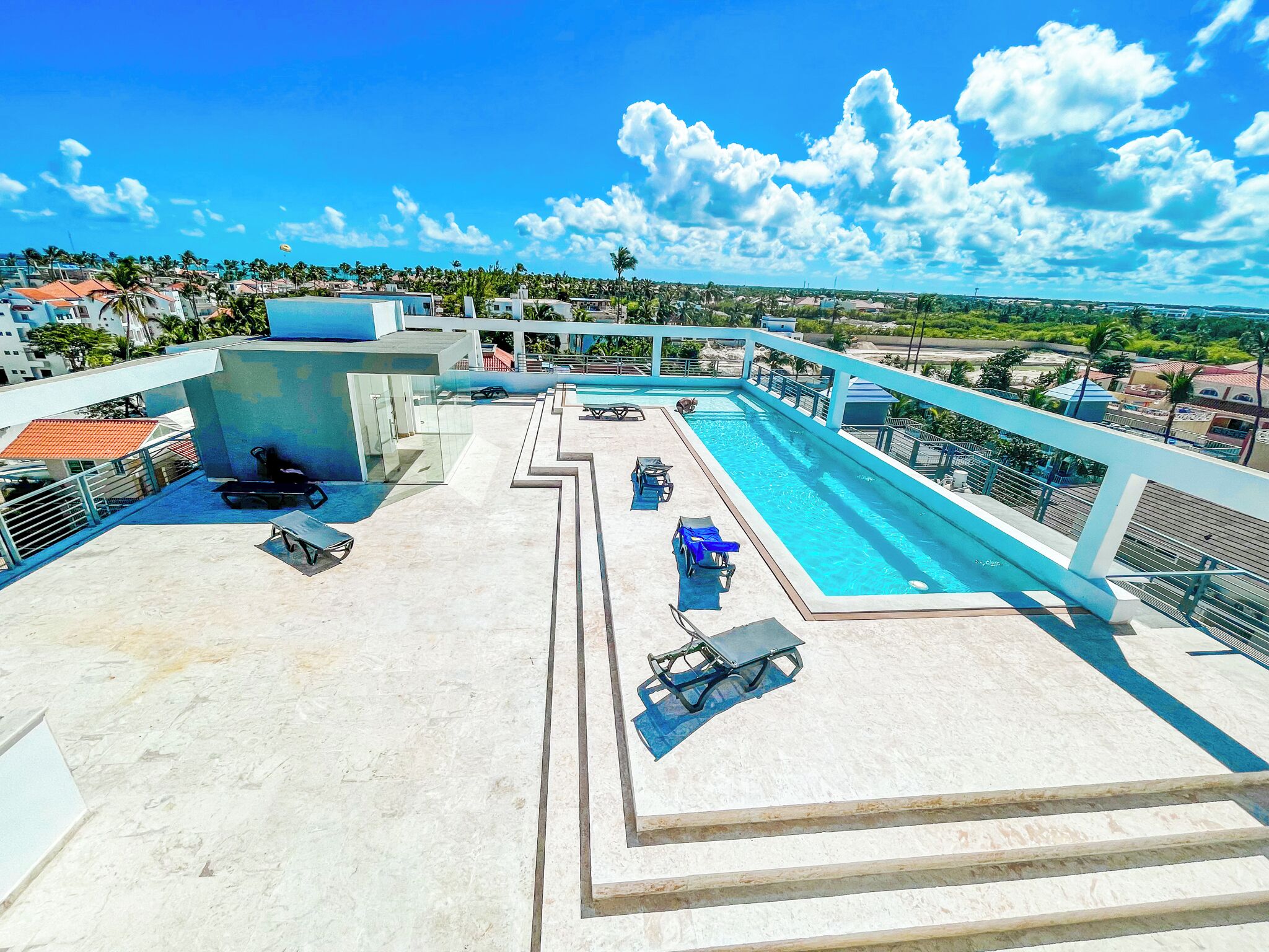 Piscina no terraço com águas azuis cristalinas, rodeada por espreguiçadeiras e vista para uma cidade costeira.