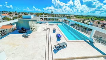 Piscina no terraço com águas azuis cristalinas, rodeada por espreguiçadeiras e vista para uma cidade costeira.