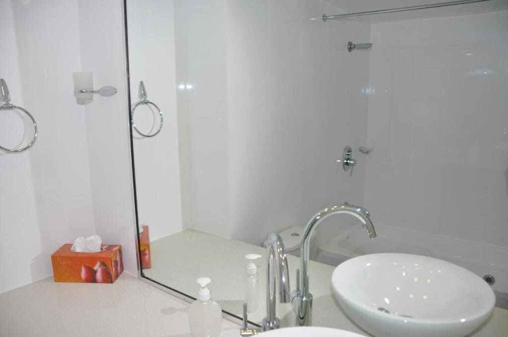 Uma casa de banho moderna com um espelho grande, uma sanita branca, área de duche e sanita.