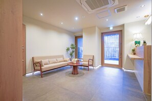 Uma sala de estar moderna com um sofá bege, duas poltronas, uma mesa de centro e um armário de madeira com uma luminária.