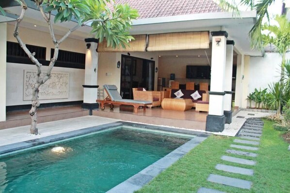 Uma área à beira da piscina com piscina, espreguiçadeiras e um espaço de estar com almofadas.