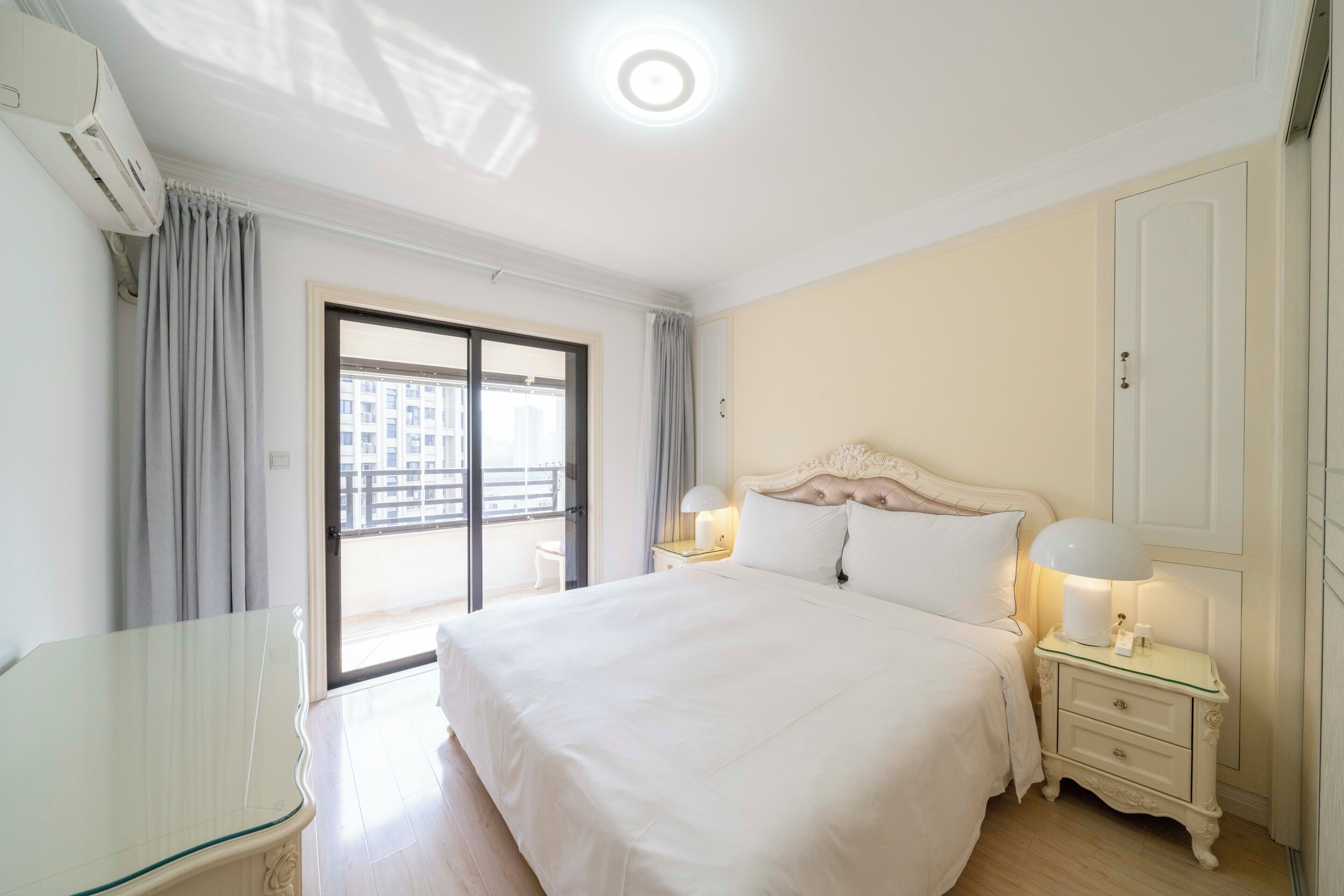 Quarto de hotel com uma cama grande, luminárias de cabeceira, uma mesa de vidro e vista para o exterior.