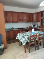 Uma cozinha com armários de madeira, uma mesa de jantar com toalha florida e um micro-ondas.