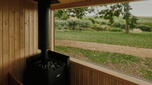 Um deck de madeira com uma lareira de madeira preta e vista para um campo gramado com árvores.