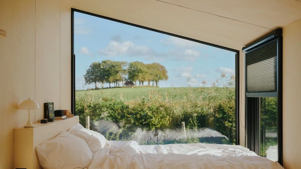 Quarto com uma janela grande, cama, mesa de cabeceira e abajur.