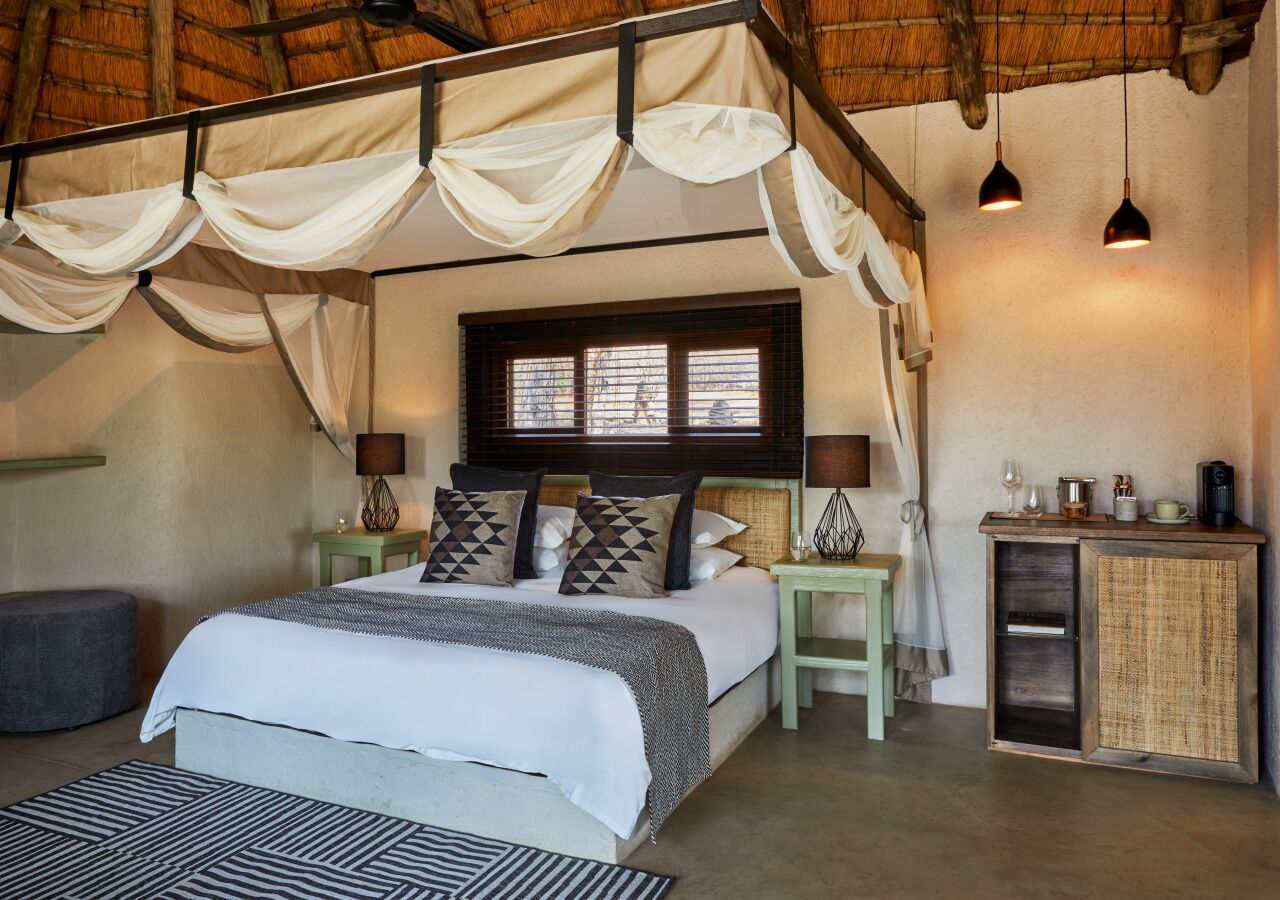 Quarto com cama de dossel, mesas de cabeceira com luminárias, um pequeno armário e janela com persianas.