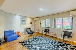 Uma sala de estar ampla com um sofá azul, um tapete estampado e várias cadeiras.