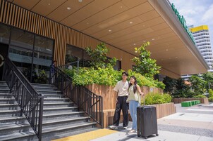 Entrada de hotel com escadaria, parede de madeira e vegetação.