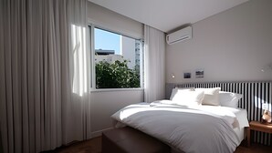 Quarto moderno com cama grande, janela com cortinas, mesa de cabeceira e radiador.