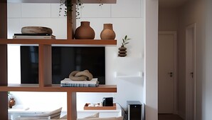 Uma sala de estar moderna com uma estante de madeira exibindo objetos decorativos, uma televisão de tela plana e um console de jogos.