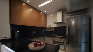 Cozinha moderna com bancada preta, eletrodomésticos de aço inoxidável e armários de madeira.