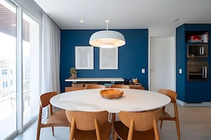 Uma área de jantar moderna com uma mesa redonda, cadeiras de madeira e uma luminária branca no teto.