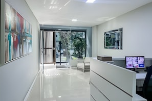 Uma área de recepção moderna com porta de vidro que dá para uma varanda, um balcão com computador e uma grande pintura abstrata na parede.