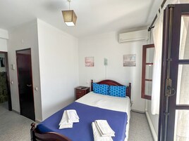 Quarto com cama, mesa de cabeceira, ar condicionado na parede e uma porta.