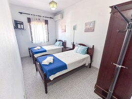 Um quarto com duas camas de madeira, cada uma com colcha azul e branca, e um guarda-roupa de madeira.