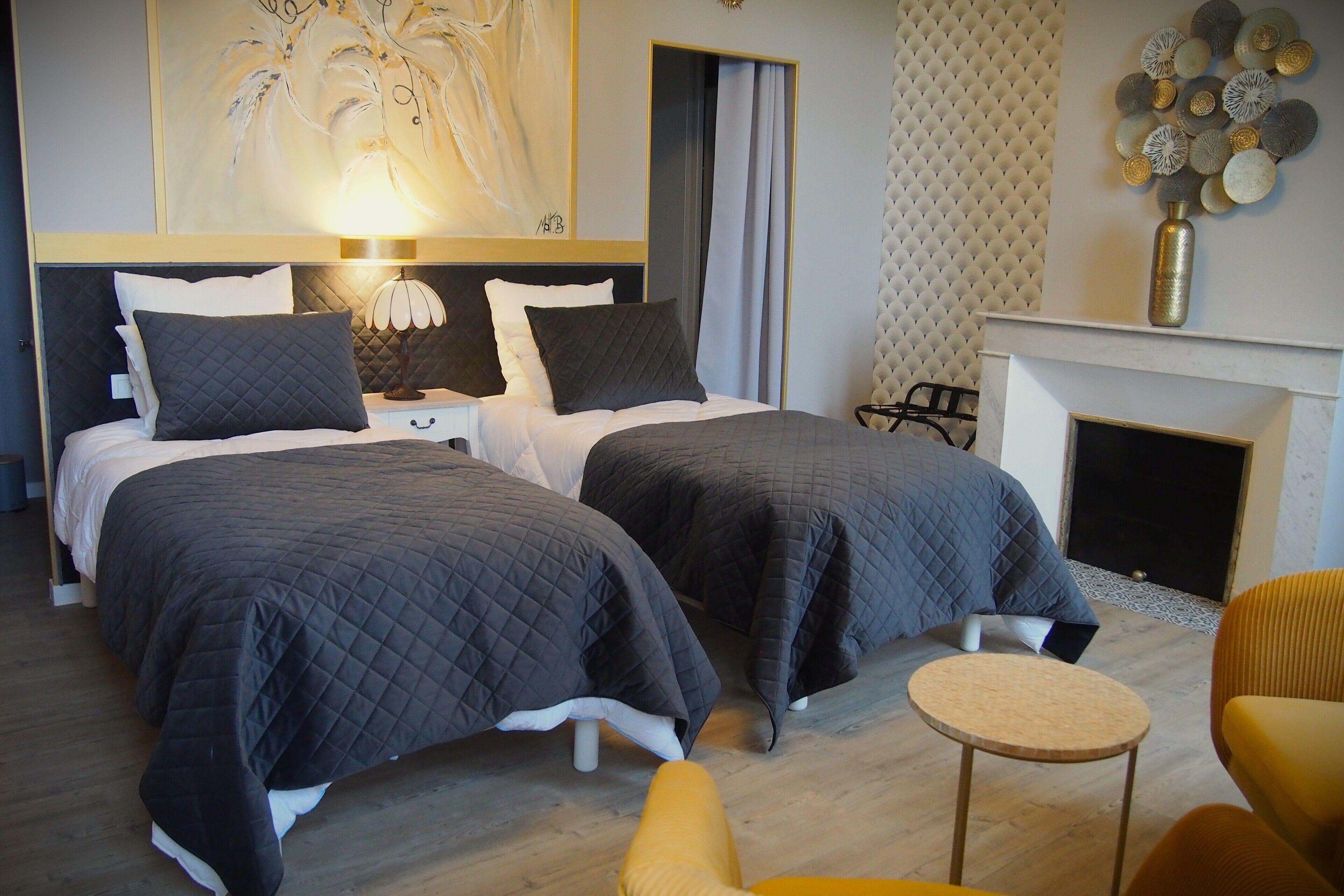 Quarto de hotel com duas camas, mesa de cabeceira, abajur, cadeira e lareira.